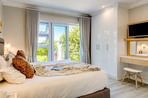 Quarto com cama grande, escrivaninha, televisão e janela com cortinas.