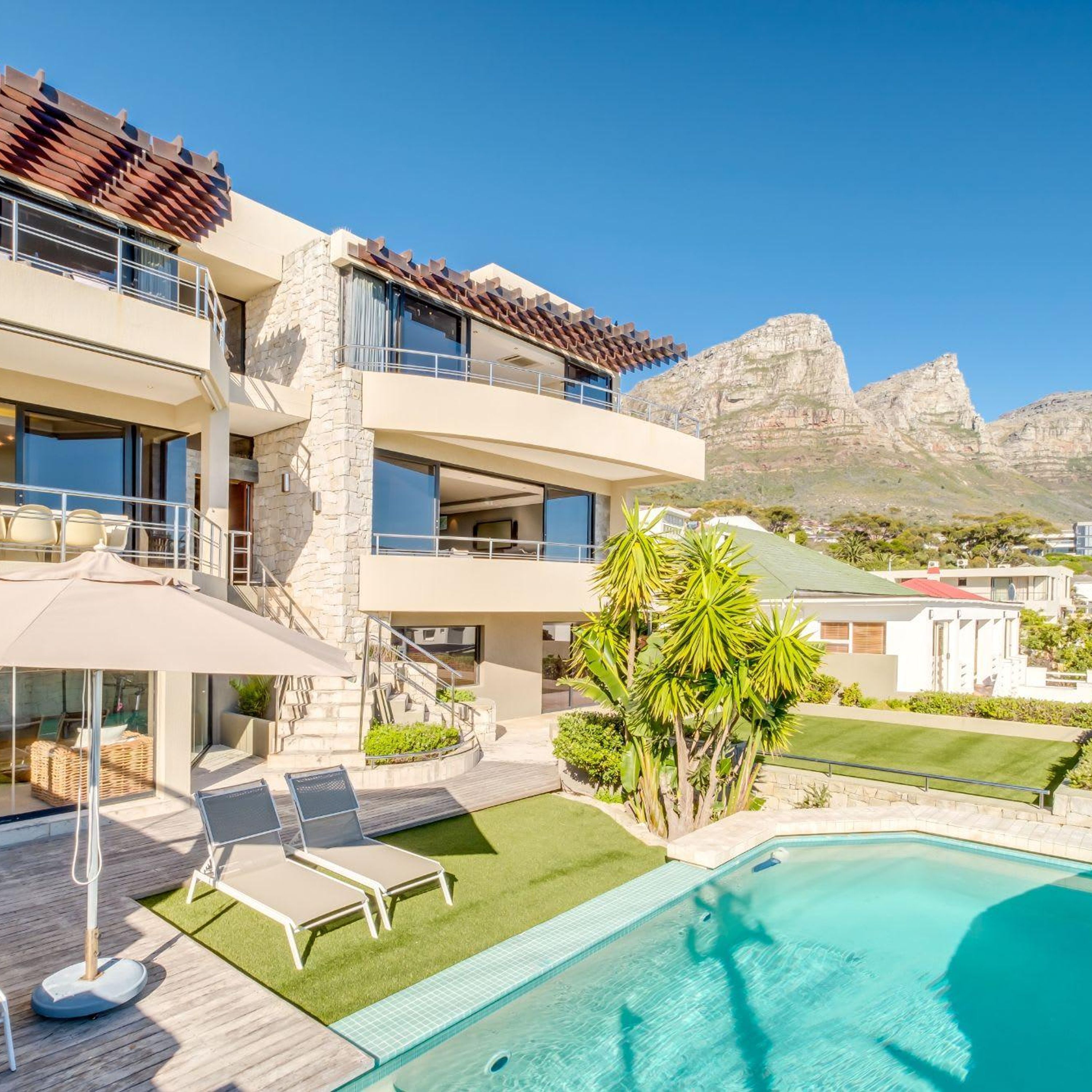 Uma casa moderna de dois andares com piscina, fachada de pedra e vista para as montanhas.