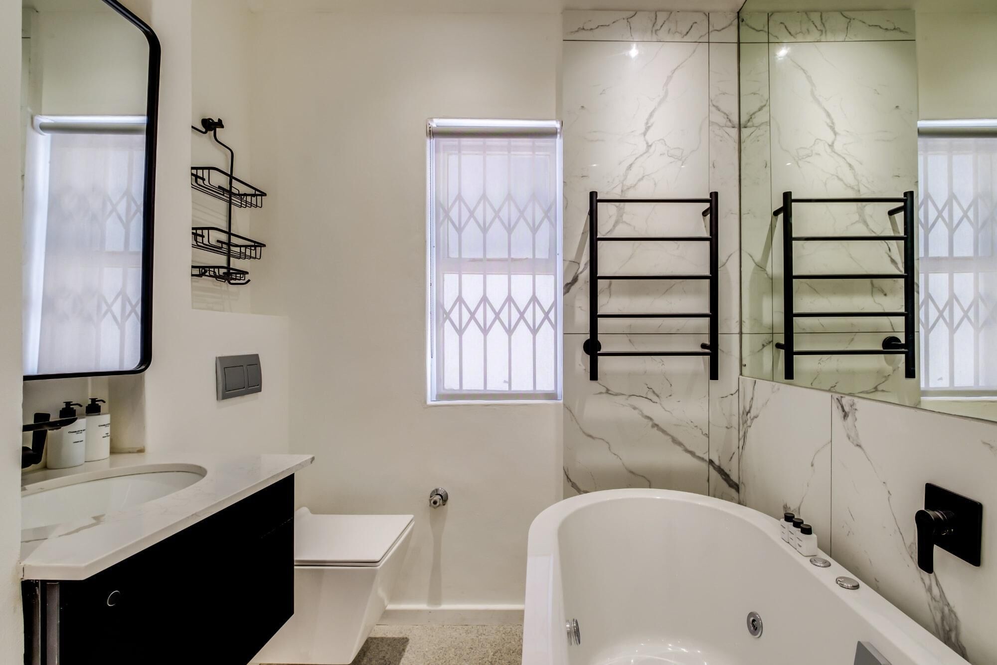 Um banheiro moderno com uma banheira branca, um porta-toalhas preto, uma pia branca e um vaso sanitário.