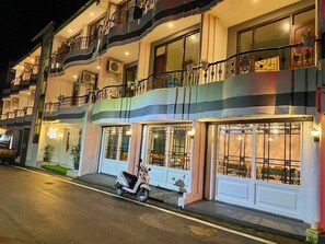 Um hotel de vários andares com varandas, janelas amplas e uma scooter estacionada na frente.