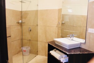 Casa de banho com cabine de chuveiro em vidro, lavatório branco e bancada de mármore.