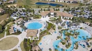 Vista aérea de um resort com várias piscinas, áreas de descanso e um campo de golfe ao fundo.