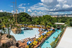 Uma grande piscina ao ar livre com várias pistas de natação, rodeada por espreguiçadeiras amarelas e guarda-sóis azuis.