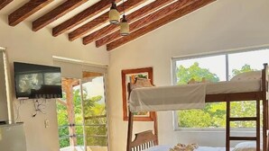 Quarto com beliches, escrivaninha com computador, televisão e grandes janelas com vista para o verde.
