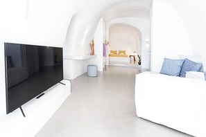 Uma sala de estar moderna com televisão de tela plana, um sofá branco e um divã com almofadas azuis.