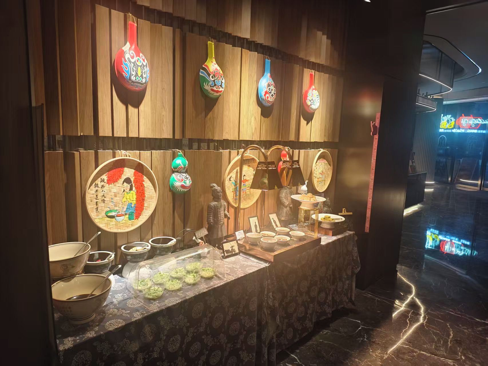 Interior de restaurante com painéis de madeira, decorações chinesas tradicionais e diversos pratos expostos em um balcão.