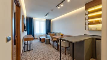Quarto de hotel moderno com cozinha compacta, sofá, mesa de jantar e uma janela grande com cortinas.