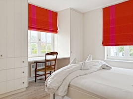 Quarto com cama, cadeira, guarda-roupa e janelas com persianas vermelhas.