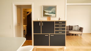 Uma sala de estar moderna com piso de madeira, um armário preto e de madeira, um sofá branco e uma mesa de centro redonda.