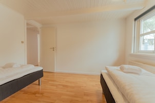 Quarto com duas camas, soalho de madeira, paredes brancas e uma janela.