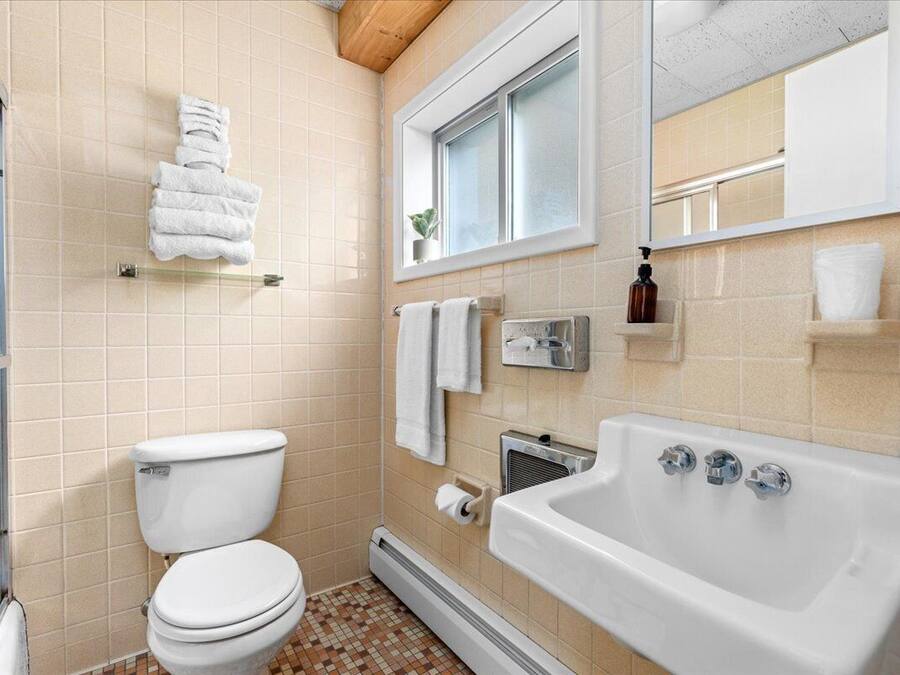 Casa de banho com sanita, uma banheira grande, janela e porta-toalhas.