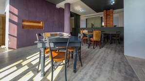 Uma sala de jantar moderna com uma parede de destaque roxa, mobiliário de madeira e vista para outro ambiente.
