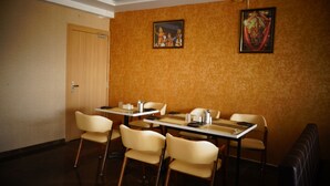 Uma sala de jantar com mesas e cadeiras, uma porta e duas molduras com imagens na parede.