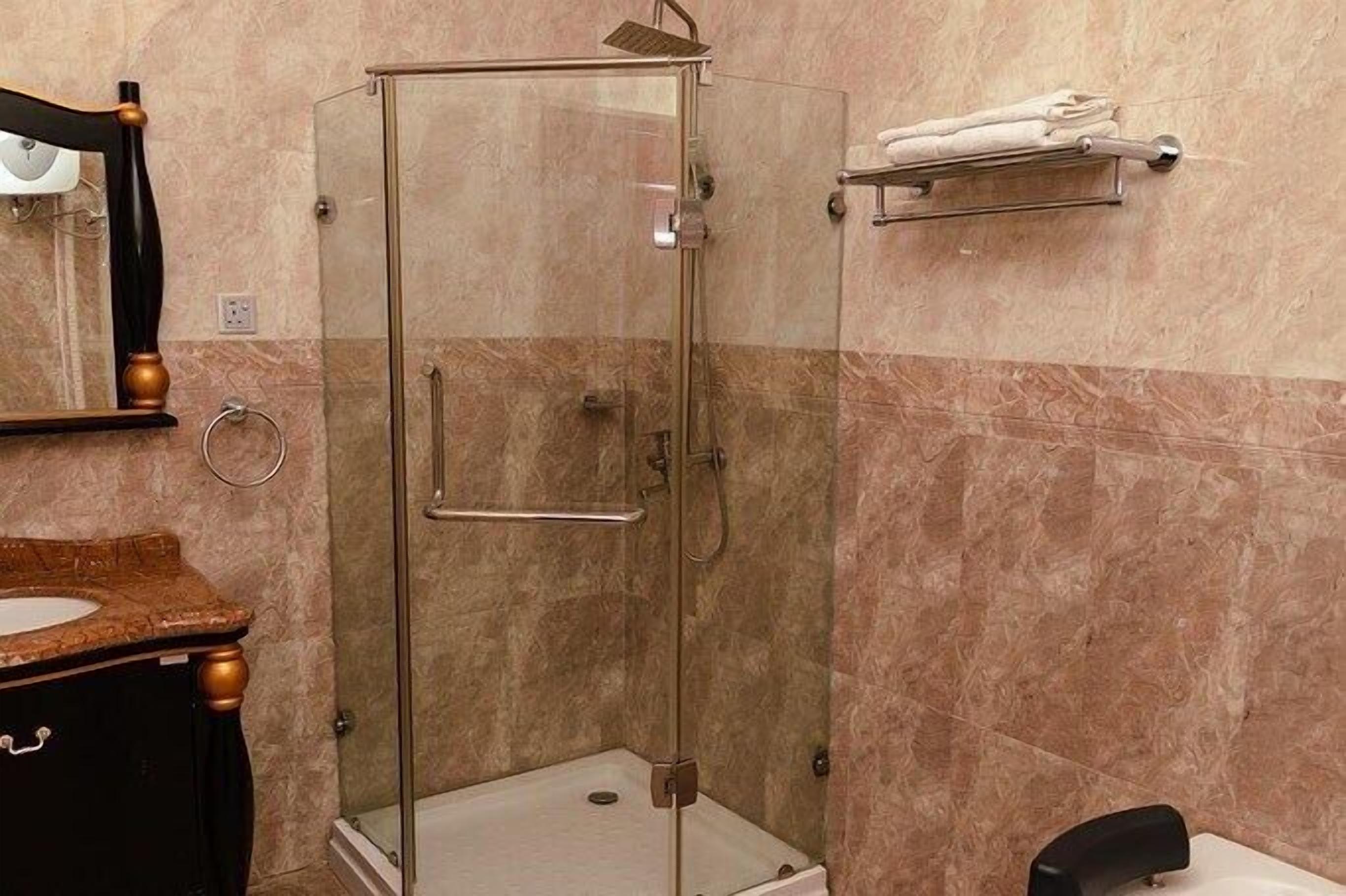 Casa de banho com cabine de duche em vidro, toucador com bancada de mármore e porta-toalhas na parede.