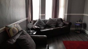 Uma sala de estar com um sofá de couro, uma mesinha e um tapete vermelho.