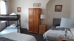 Quarto de hotel com beliches, um guarda-roupa, mesa de cabeceira com abajur e um pequeno armário com controle remoto.