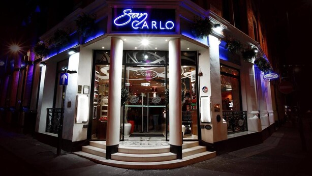Fachada com um letreiro de neon que diz "San Carlo" e uma placa indicando "Aberto o Dia Todo".