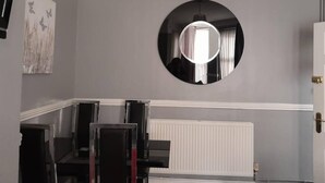 Quarto com um espelho redondo na parede, um radiador embaixo e uma porta à direita.