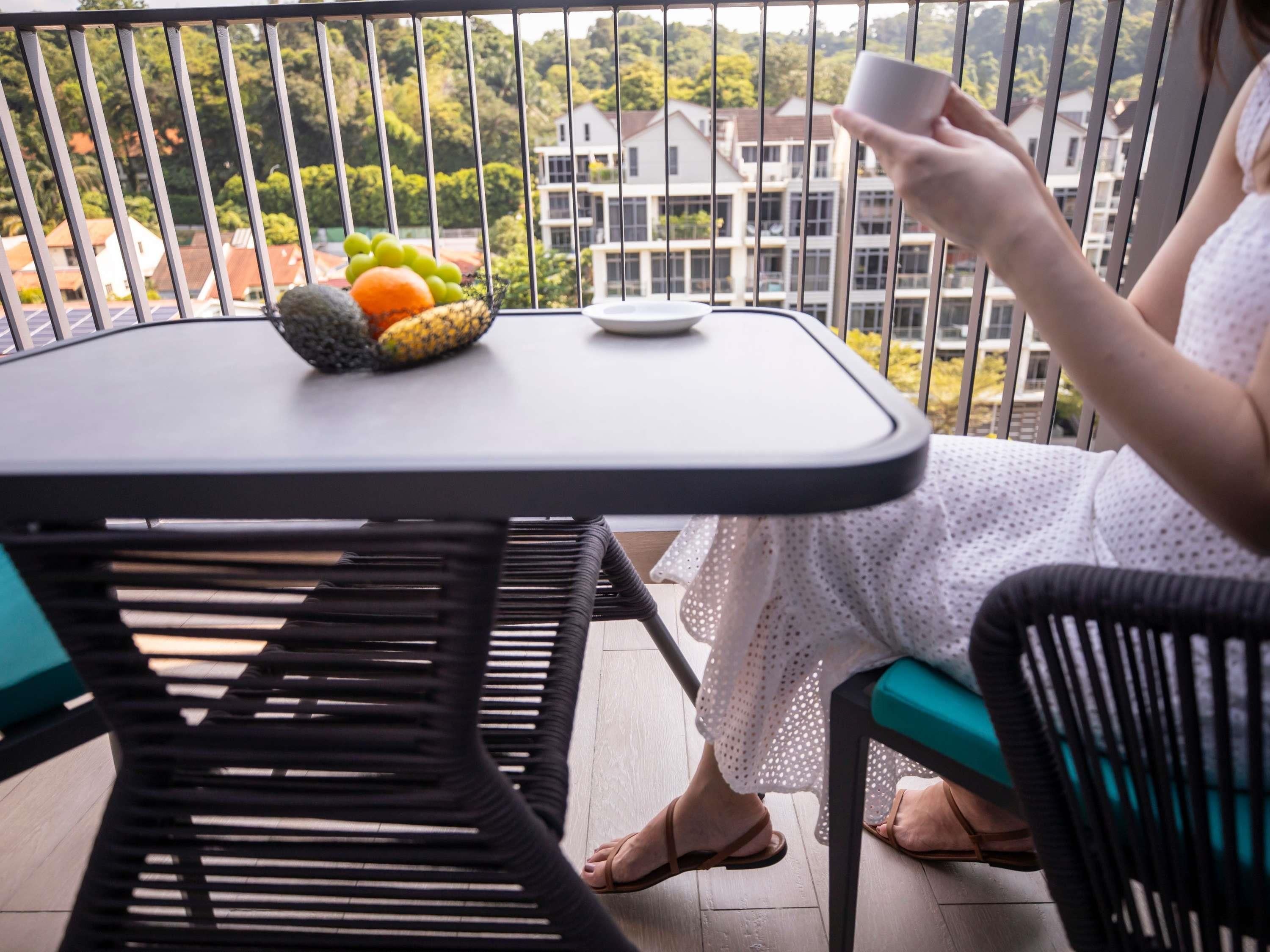 Uma pessoa sentada à mesa com uma cesta de frutas, numa varanda com guarda-corpo.