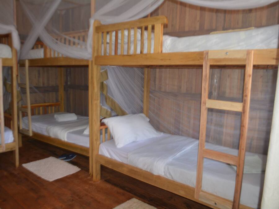 Um quarto com beliches, piso de madeira e mosquiteiro.