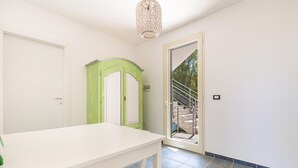 Quarto com uma mesa branca, uma porta verde e uma escada que dá para o exterior.