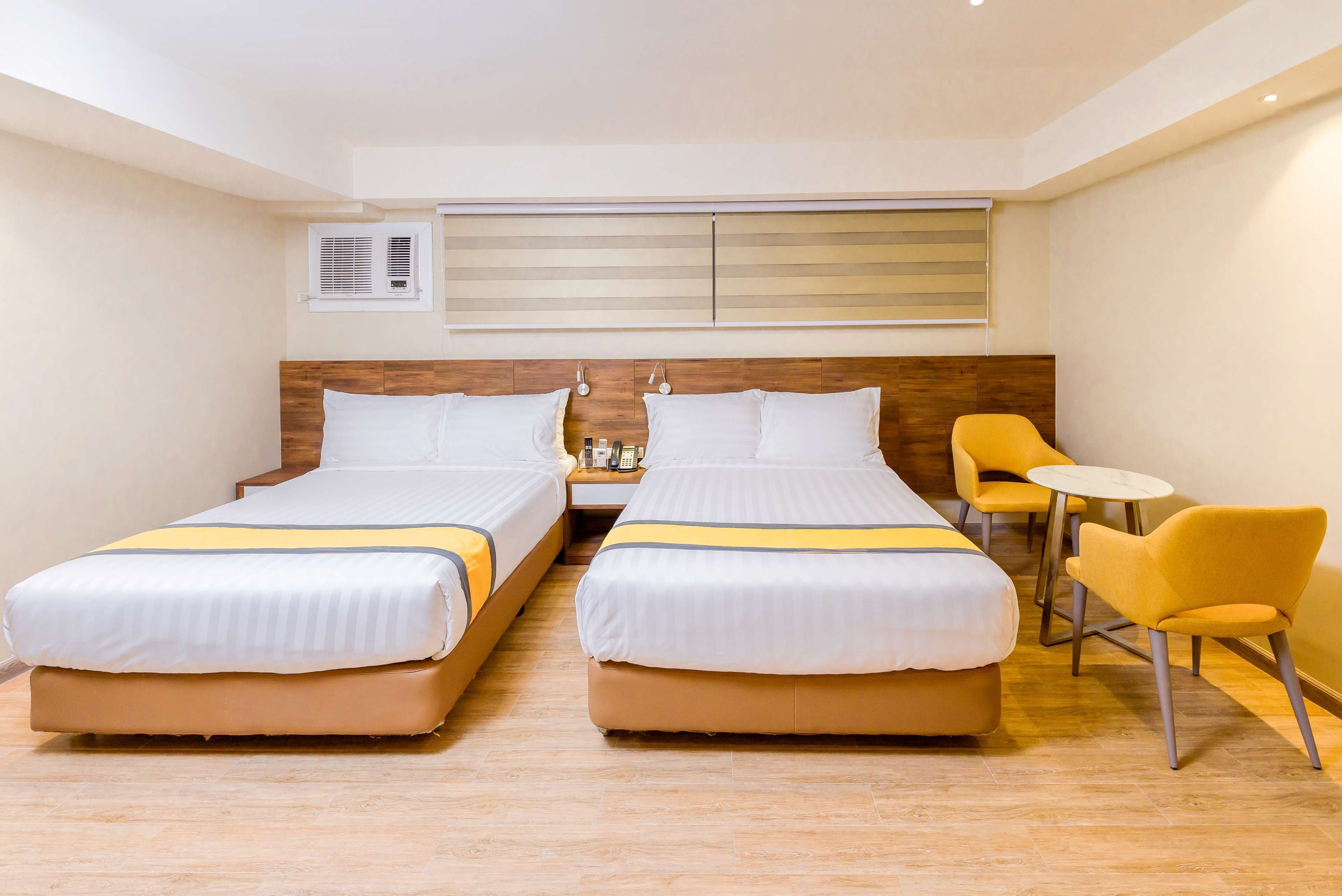 Quarto de hotel com duas camas, uma mesa pequena e uma cadeira.
