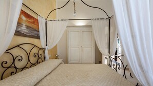 Quarto com cama de dossel, um quadro na parede e uma porta branca ao fundo.