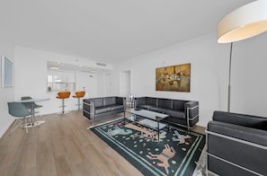 Uma sala de estar moderna com uma mesa de centro de vidro, sofás de couro e um tapete colorido.