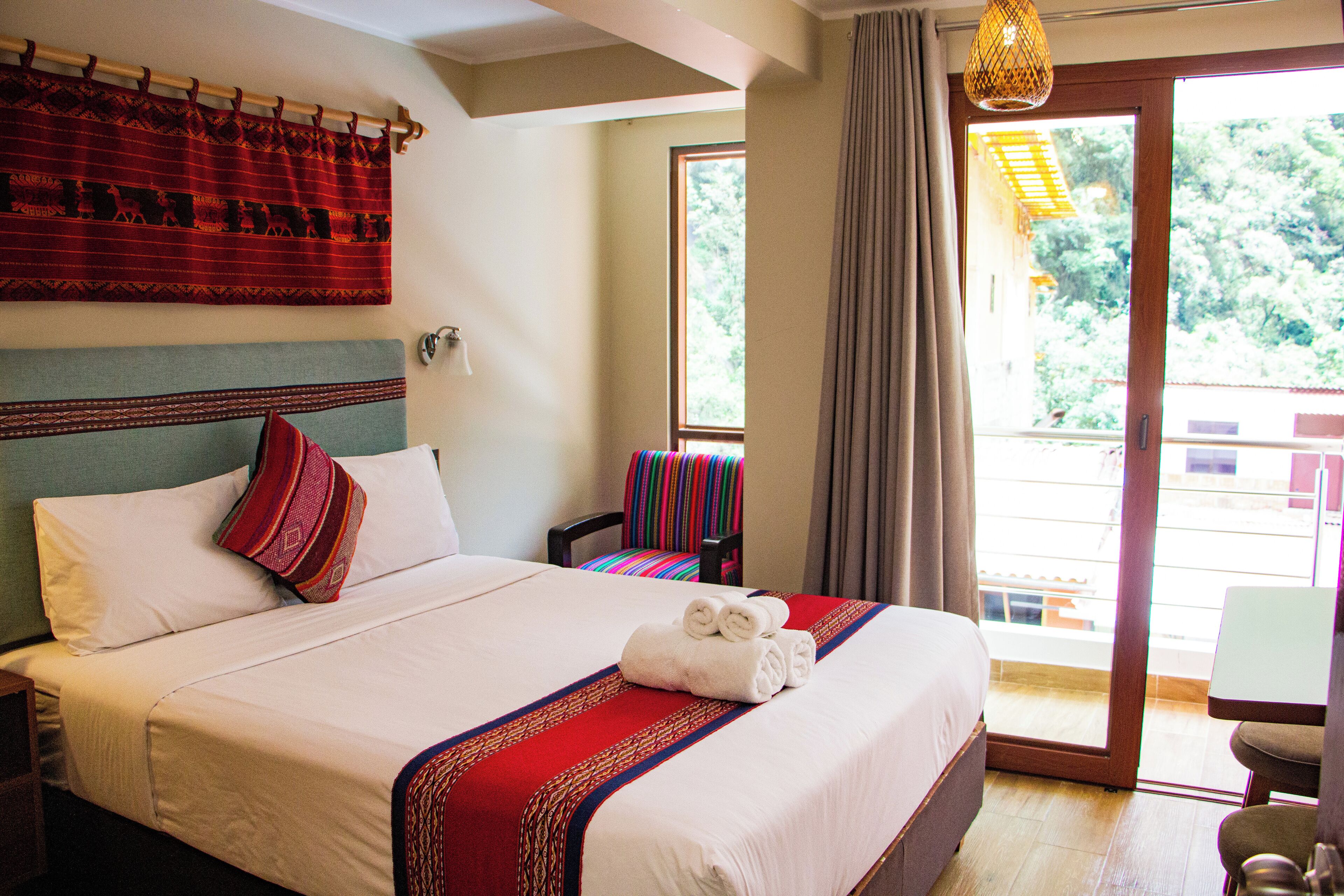 Quarto de hotel com uma cama grande, uma cadeira, uma mesa e uma varanda com vista para o verde.