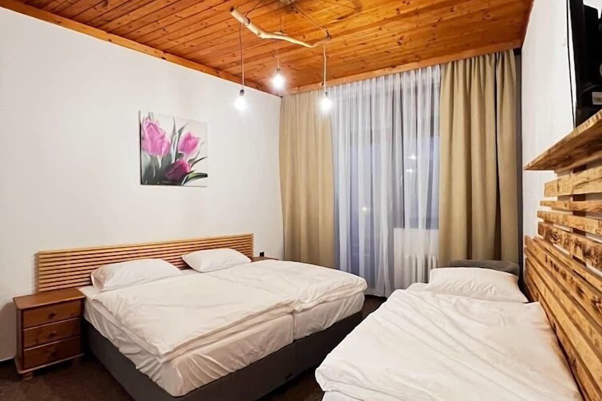 Quarto com duas camas, teto de madeira, um quadro de flores e uma janela com cortinas.