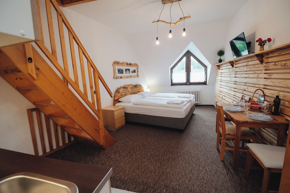 Quarto com cama, escada de madeira, mesa de jantar com cadeiras, janela e radiador.