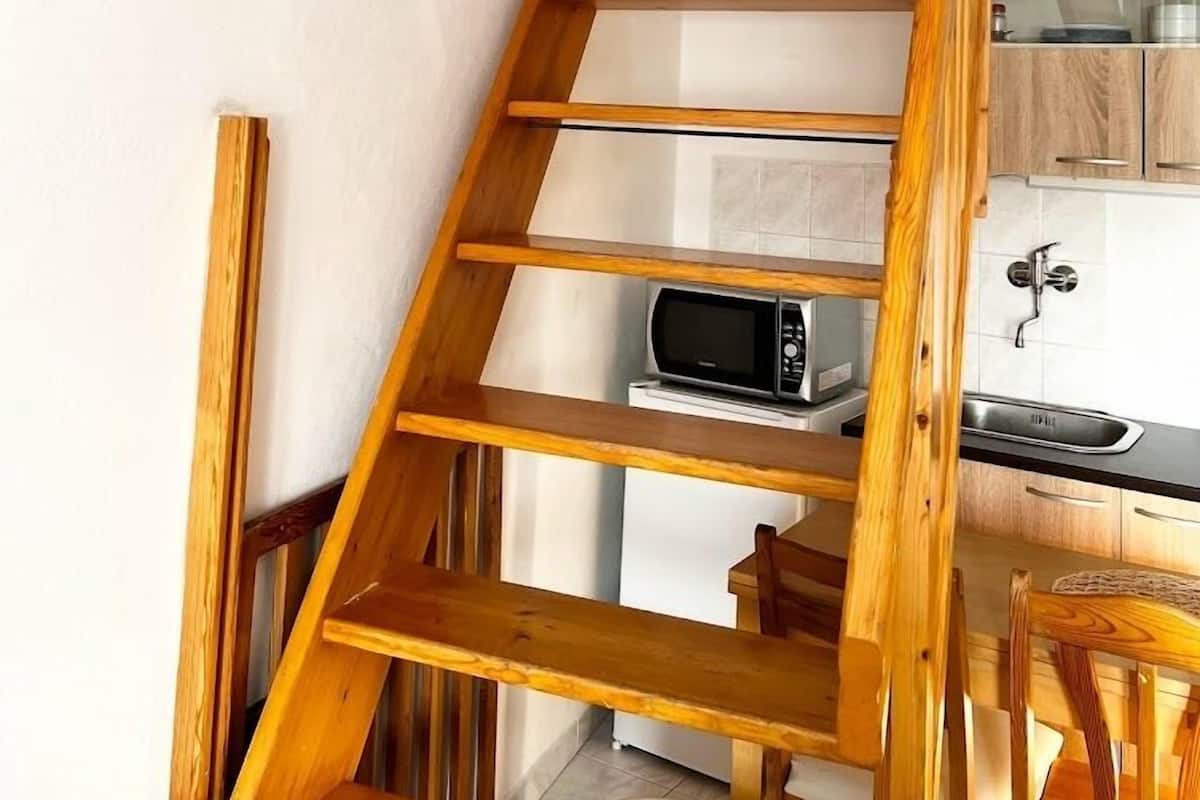 Escada de madeira que dá acesso a uma cozinha com micro-ondas e armários.