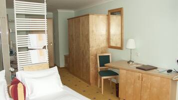 Quarto de hotel com cama, escrivaninha, cadeira, guarda-roupa e espelho.