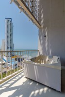 Uma varanda com hidromassagem, corrimão e vista para o oceano e edifícios.