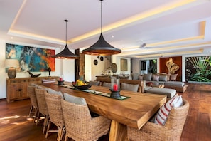 Uma sala de estar espaçosa com uma mesa de jantar de madeira, cadeiras de vime e um amplo sofá.