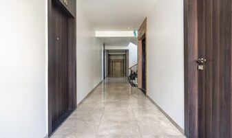 Um corredor longo e estreito, com portas de madeira escura de ambos os lados e chão de azulejos.
