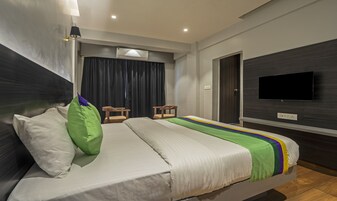 Quarto de hotel moderno com uma cama grande, uma TV de tela plana na parede, uma pequena cadeira de madeira e uma mesa.