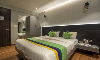 Quarto de hotel moderno com uma cama grande, uma mesinha de cabeceira com chaleira e um espelho sobre a cama.