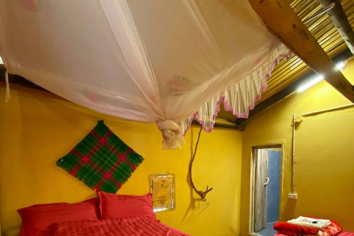 Quarto com cama coberta por um cobertor vermelho, mosquiteiro e uma pequena mesa com tecido vermelho.