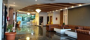 Um hall moderno com piso refletivo, área de estar com sofás de couro e uma grande planta em vaso.
