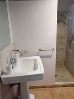 Casa de banho com uma pia branca, espelho e zona de duche.