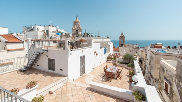Terraço no telhado com área de refei ções, uma torre sineira e vista para o mar.