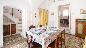 Uma sala de jantar com mesa posta para seis, uma escadaria e vista para outro cômodo.