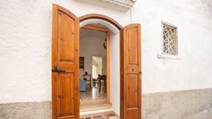 Uma entrada com portas de madeira que dá para um espaço interior com piso ladrilhado e uma área de refeições visível.