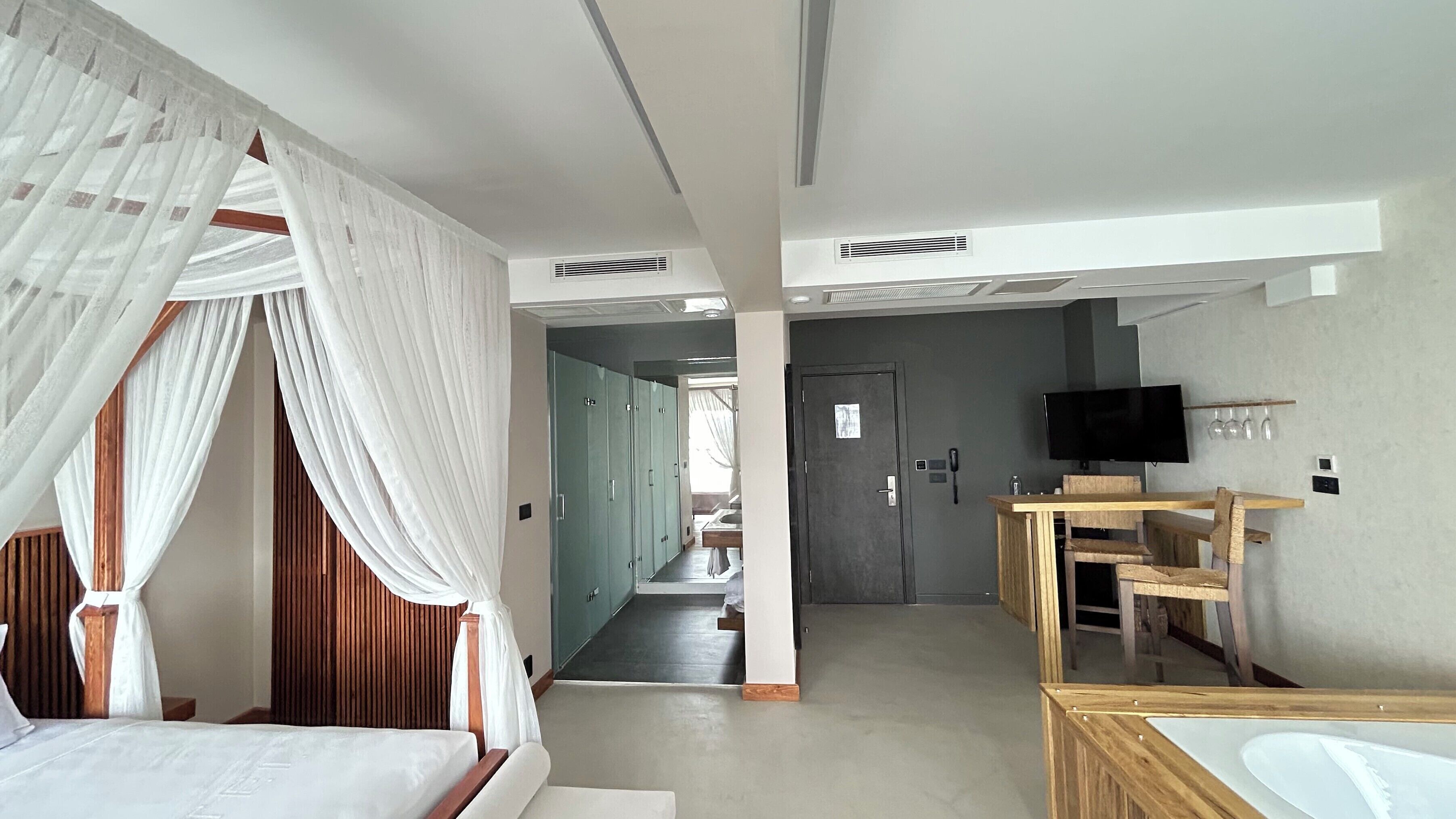 Quarto de hotel com uma cama, um banco de madeira, uma televisão e banheiro com banheira.