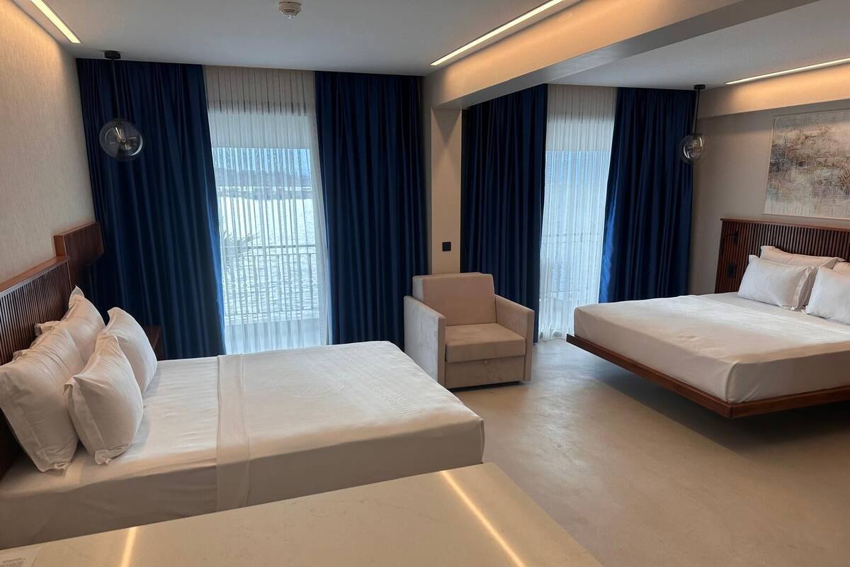 Quarto de hotel com duas camas, uma cadeira e uma janela grande com cortinas.