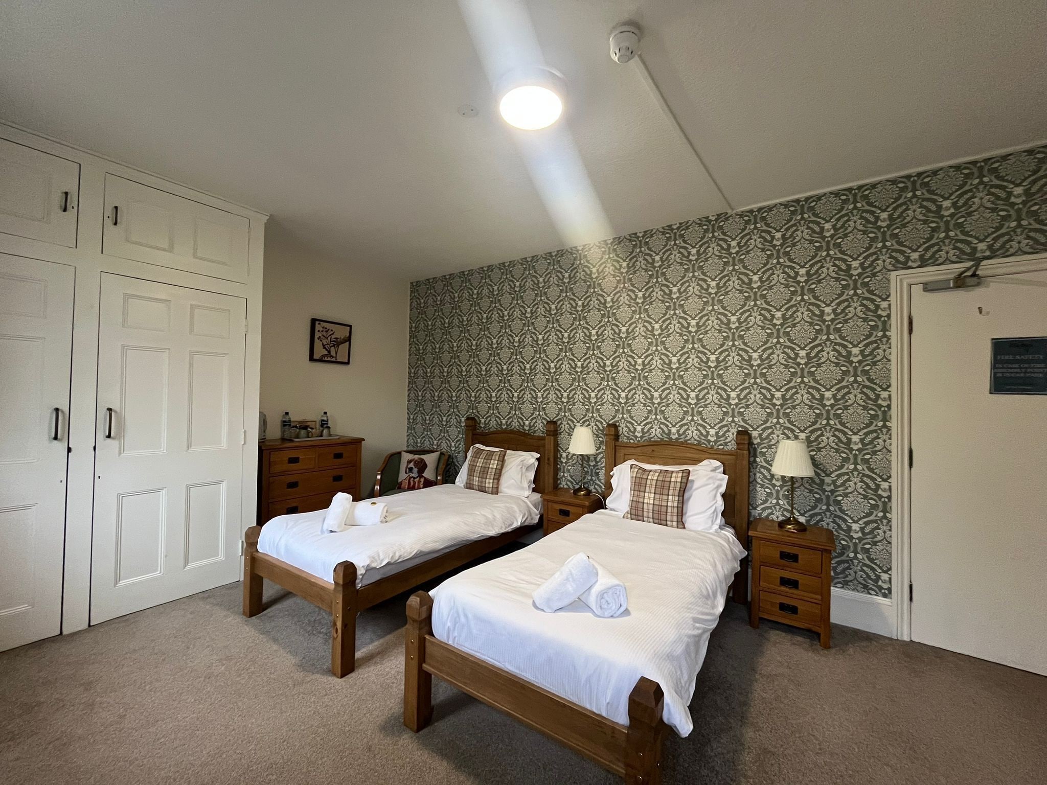 Quarto com duas camas de madeira, um guarda-roupa, uma mesa de cabeceira e papel de parede estampado.