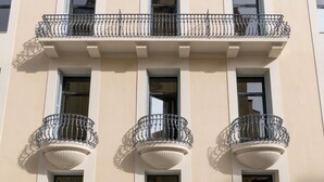 Fachada de edifício com três varandas, cada uma com grades de ferro forjado e parapeito branco.