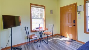 Quarto com piso de madeira, uma mesa com duas cadeiras, televisão e porta com janela.
