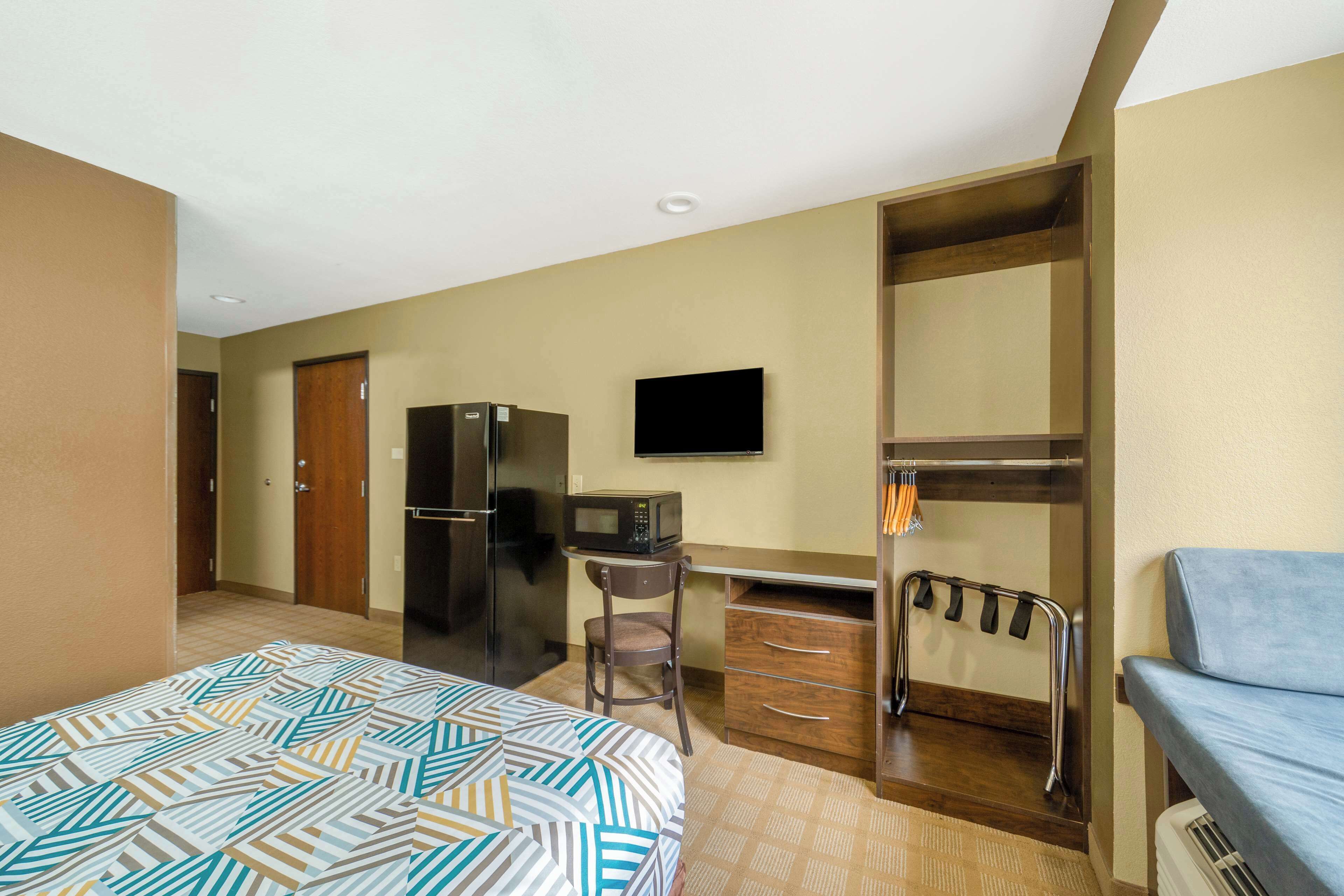Quarto de hotel com cama, escrivaninha com cadeira, frigorífico, televisão e área de estar com um banco.